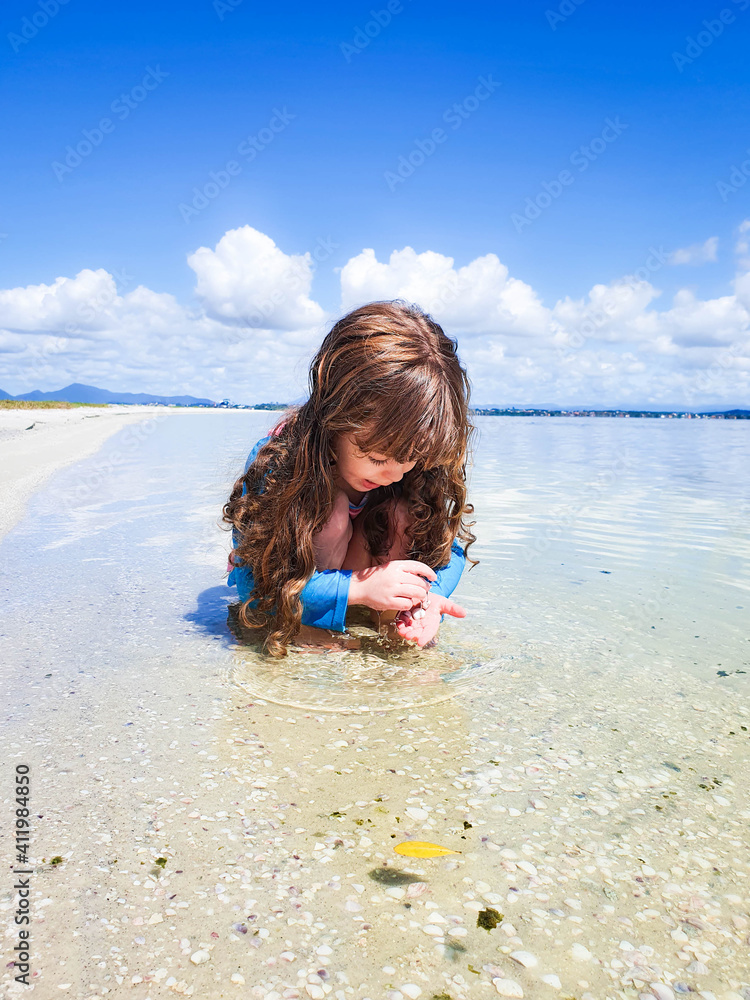 Girl collecting pebbles in shallow water on beach, Rio de Janeiro ...