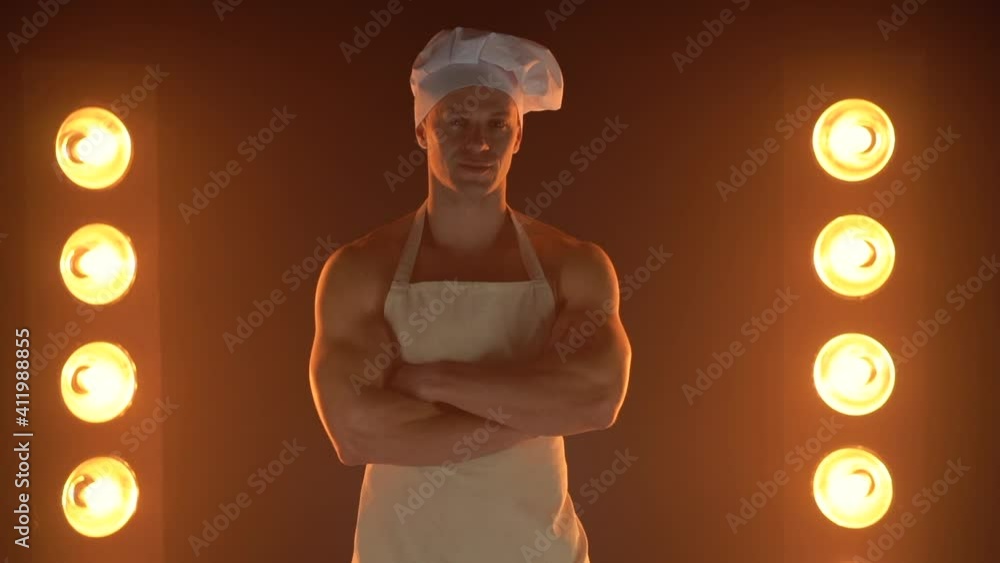 Portrait of muscular chef wearing white apron and chef hat, posing with ...