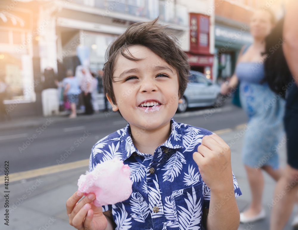 Smiling Kid eating cotton candy with blurry people walking on street ...
