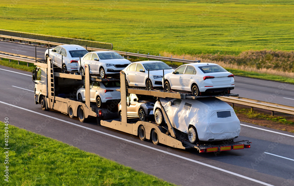 Car carrier trailer transports cars on highway on sunset background ...