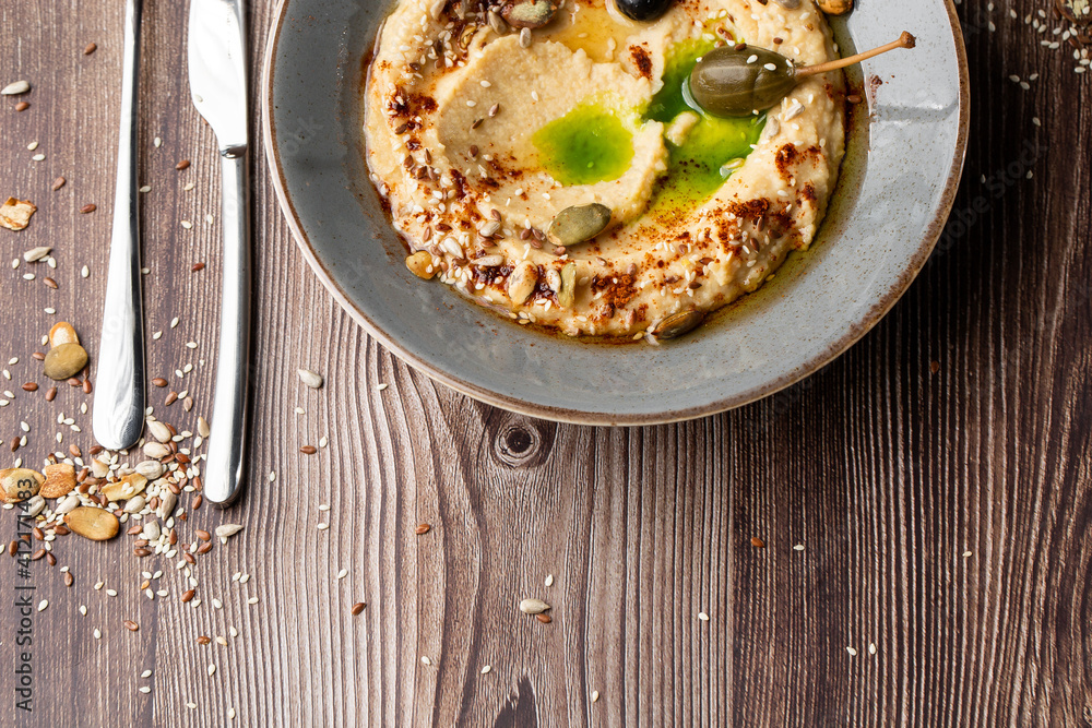 Hummus in a grey bowl seasoned with sunflower and pumpkin seeds, sesame ...