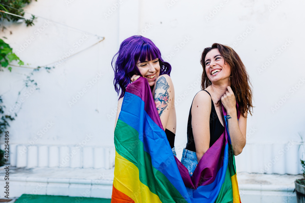 Two women with rainbow flag on a backyard. Couple Young lesbian girls ...