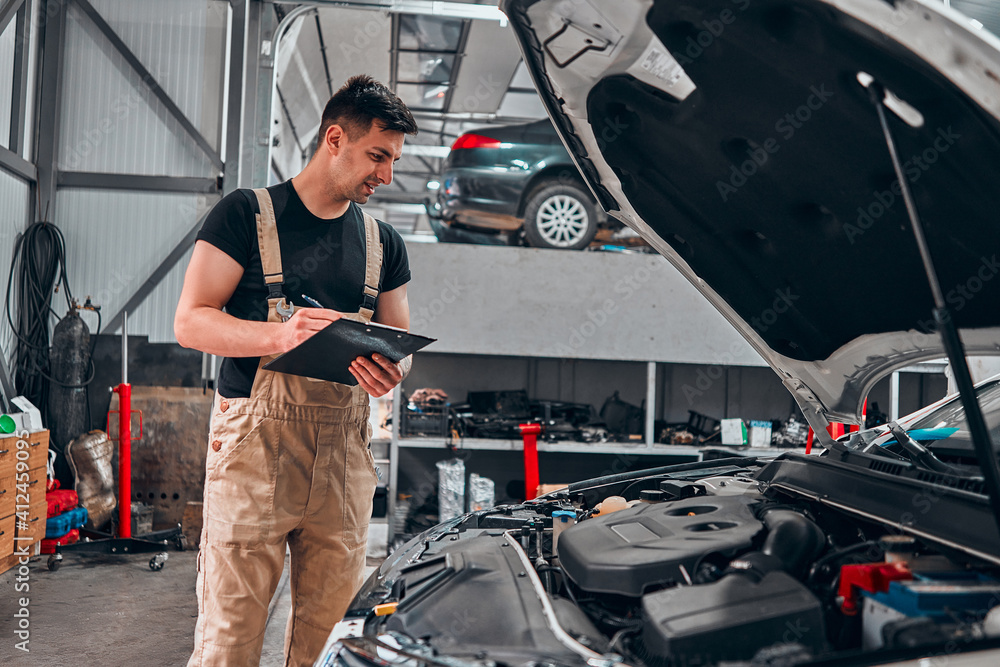 Mechachic checking on a car engine and taking notes. Stock Photo ...