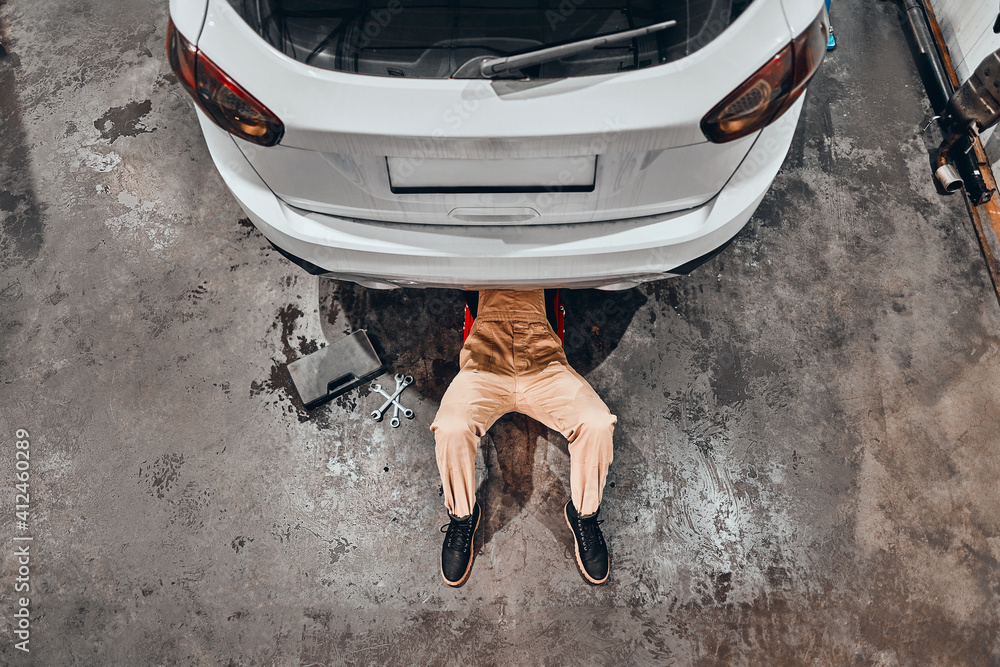 Mechanic lying and working under car at the repair garage. Stock Photo ...