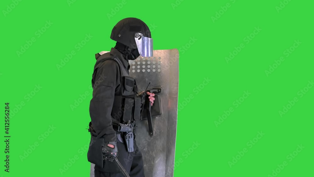 Heavily armored policeman with a shield and a baton walking on a Green ...