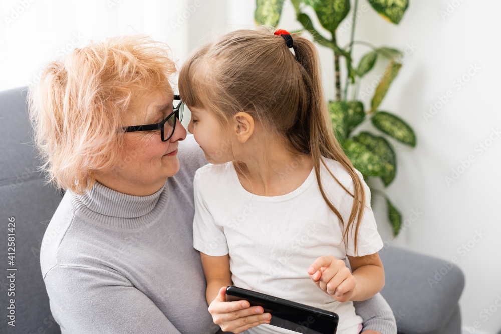 Happy grandmother and granddaughter using phone together, sitting on ...