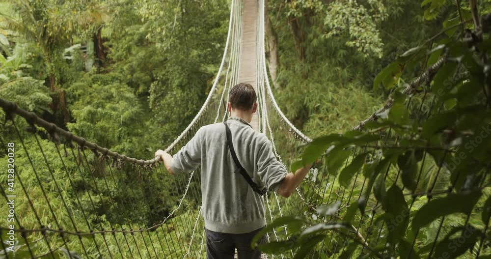 Back close up view of a man making his way across an unstable rope ...