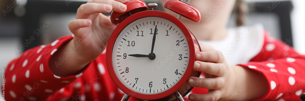 Little girl in background presses button of red alarm clock with her ...