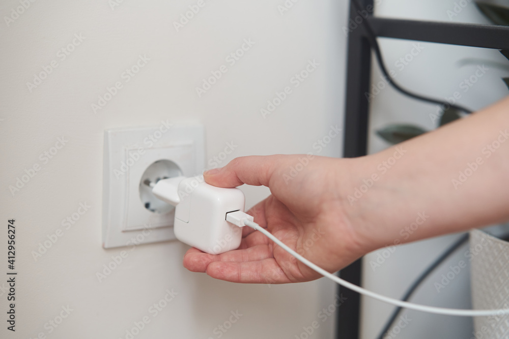 A young girl inserts a plug into an outlet. Young woman plugs the phone ...