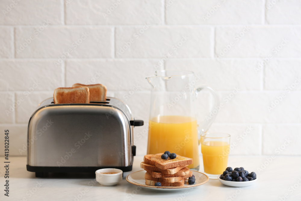 Modern toaster and tasty breakfast on white table near brick wall Stock ...