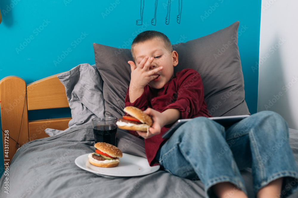 little boy using digital tablet and eating junk food while laying on ...