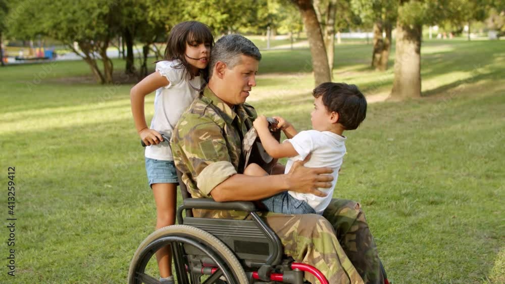 Disabled military dad playing with kids in park, holding boy in arms on ...