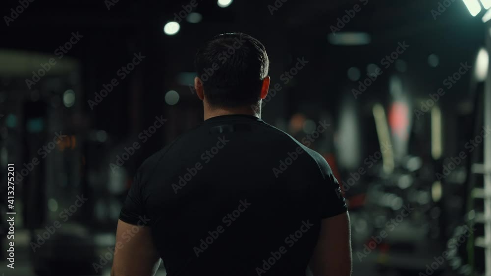 Muscular man in black t-shirt walking in dark gym, unrecognizable ...