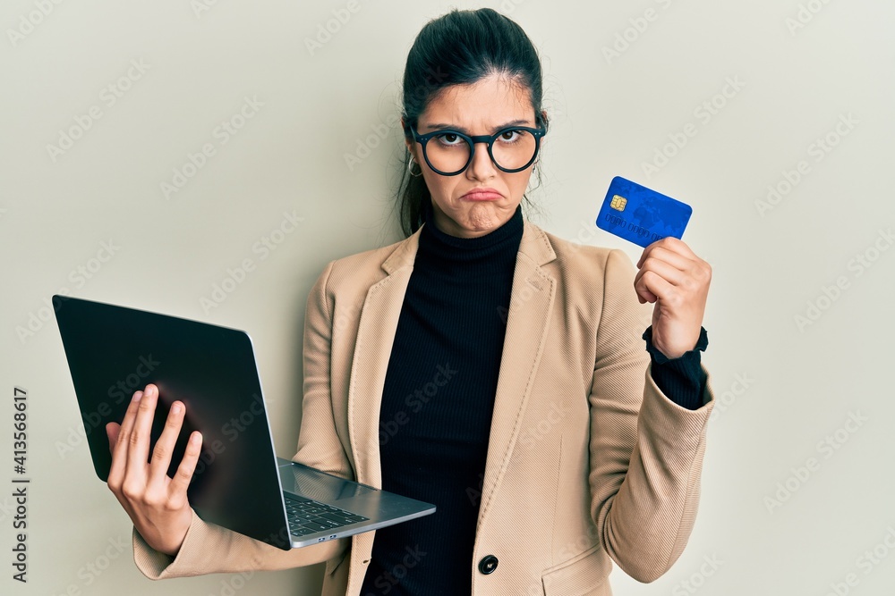 Young hispanic woman wearing business style holding laptop and credit ...