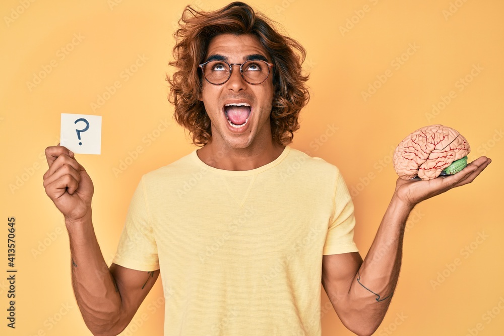 Young hispanic man holding brain and question mark angry and mad ...