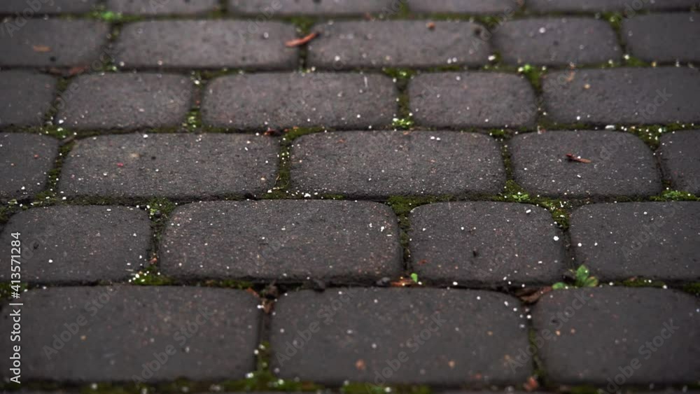 White snowflakes falling on the dark paving stones in slow motion ...