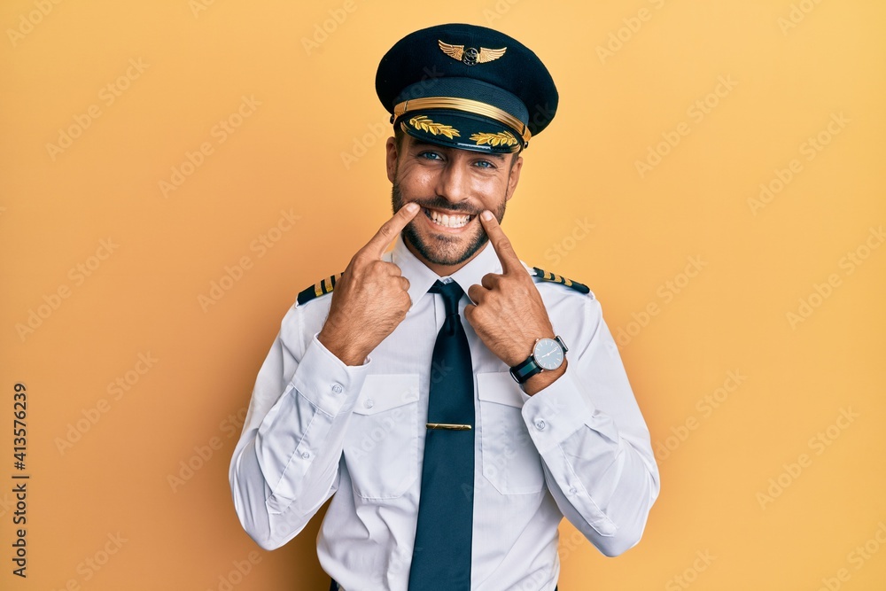 Handsome hispanic man wearing airplane pilot uniform smiling with open ...