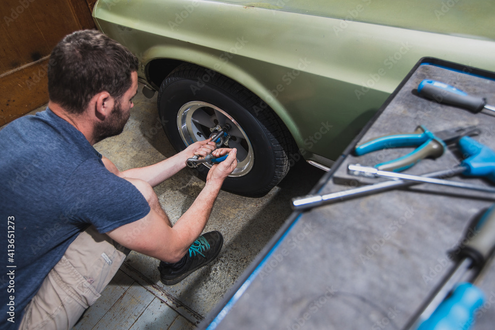 Young man removing wheels or tires from an old vintage car from the 60s ...
