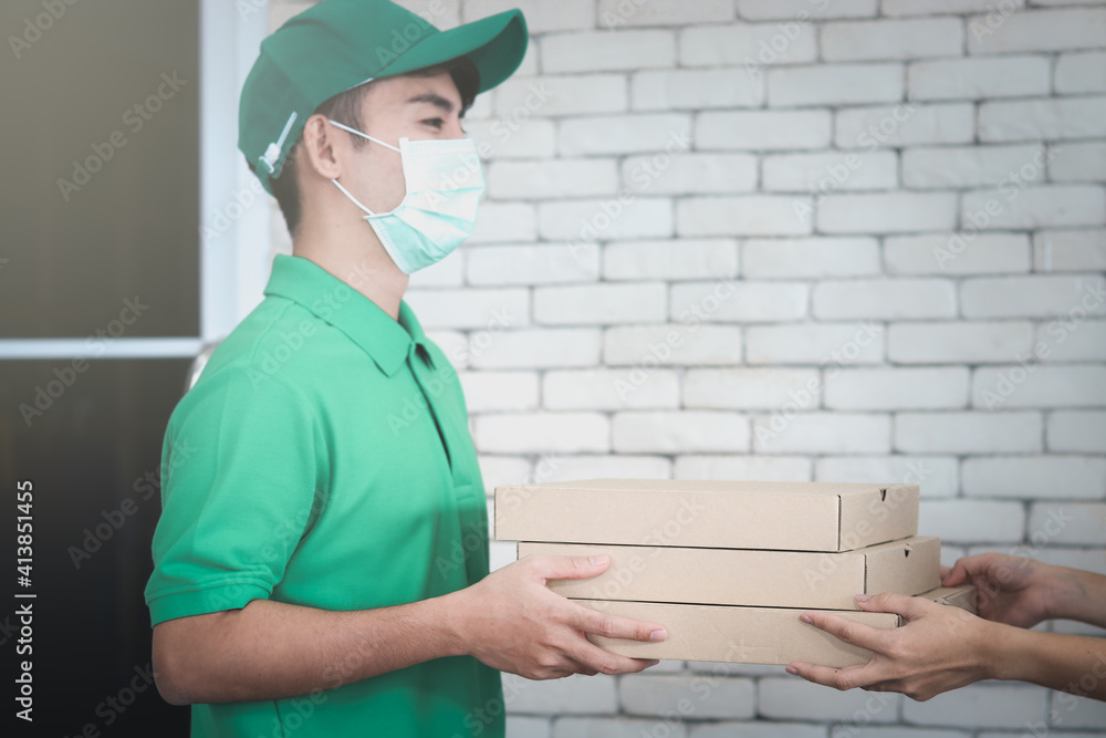 Young Asian delivery man in green T-shirt uniform and cap wearing face ...