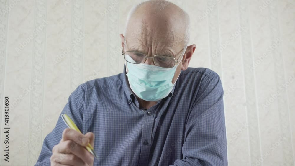 Gray haired old man with glasses sits at table and writes letter with ...