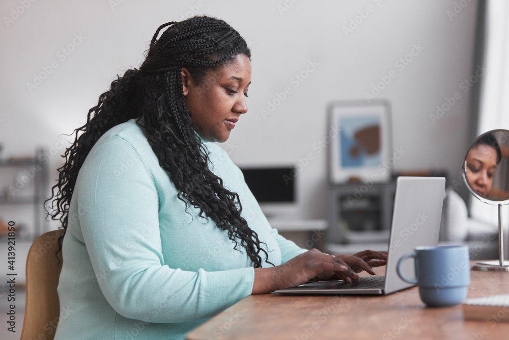 Side view portrait of curvy African American woman using laptop at desk ...