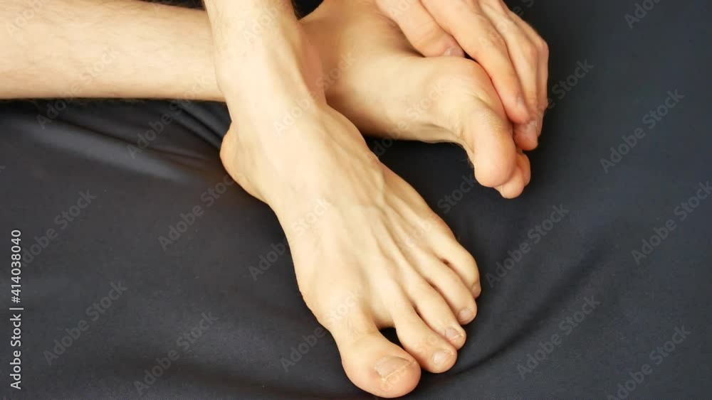 Close-up of the feet of a man lying on a bad and the hand scratching ...