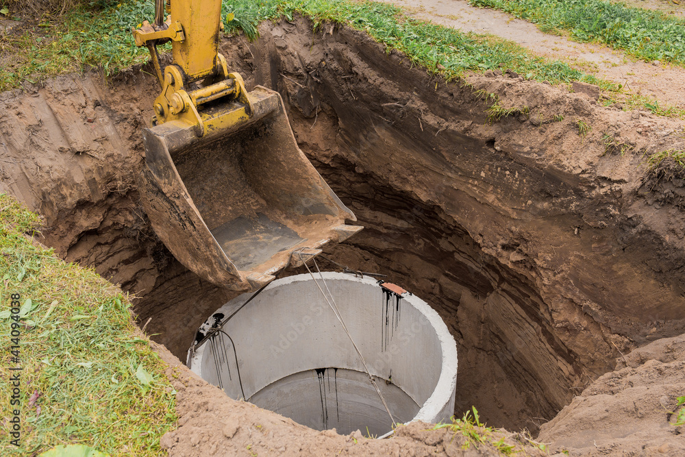 Excavator with a bucket, lowering into the pit on steel cables concrete ...