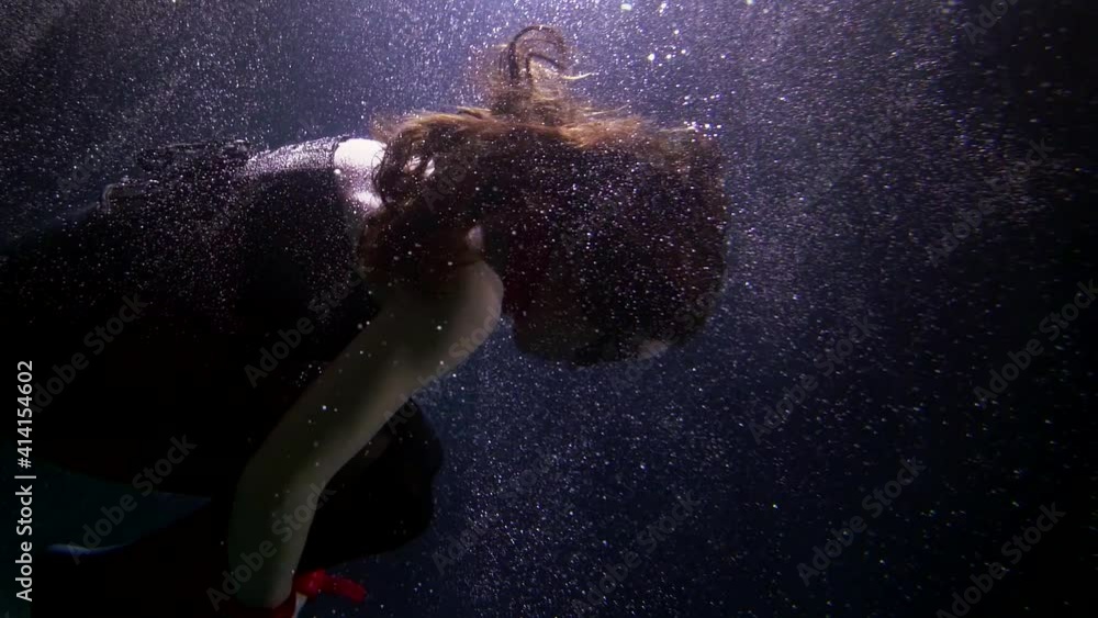 A beautiful woman is deep under the water on a dark background ...