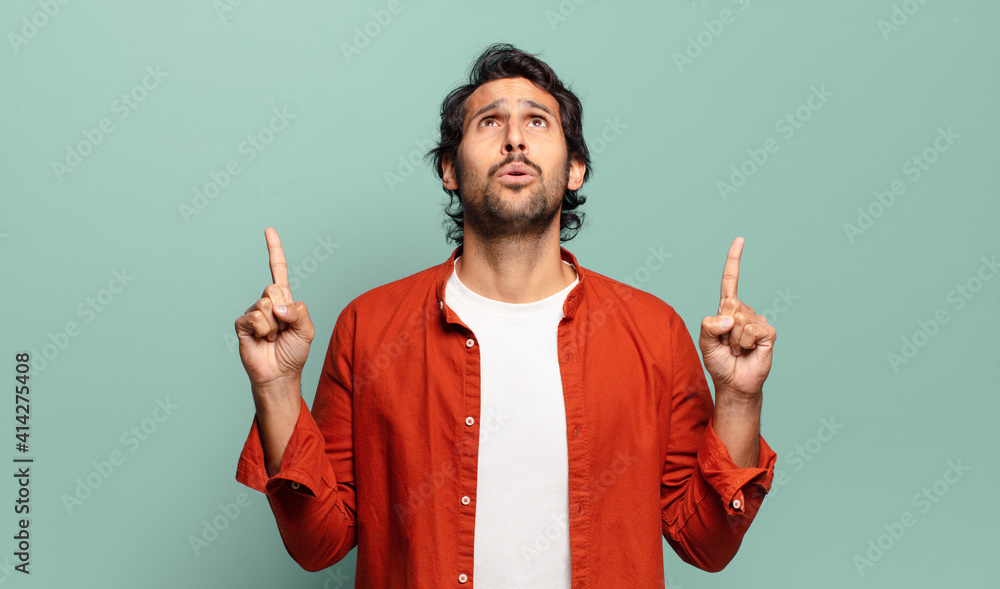 young handsome indian man feeling awed and open mouthed pointing ...