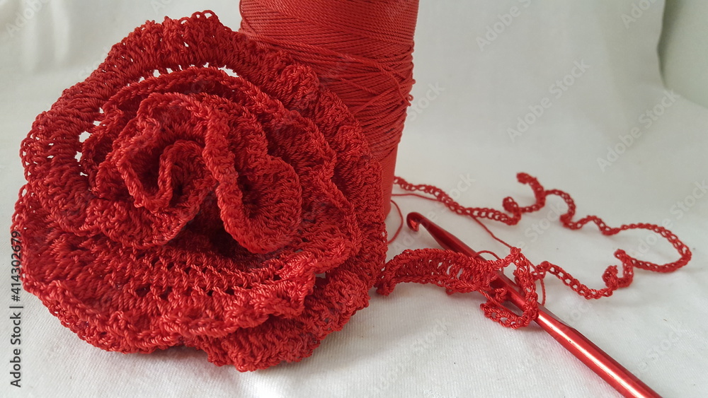 A red cone of crochet thread and a rose, a finished piece of crocheted ...