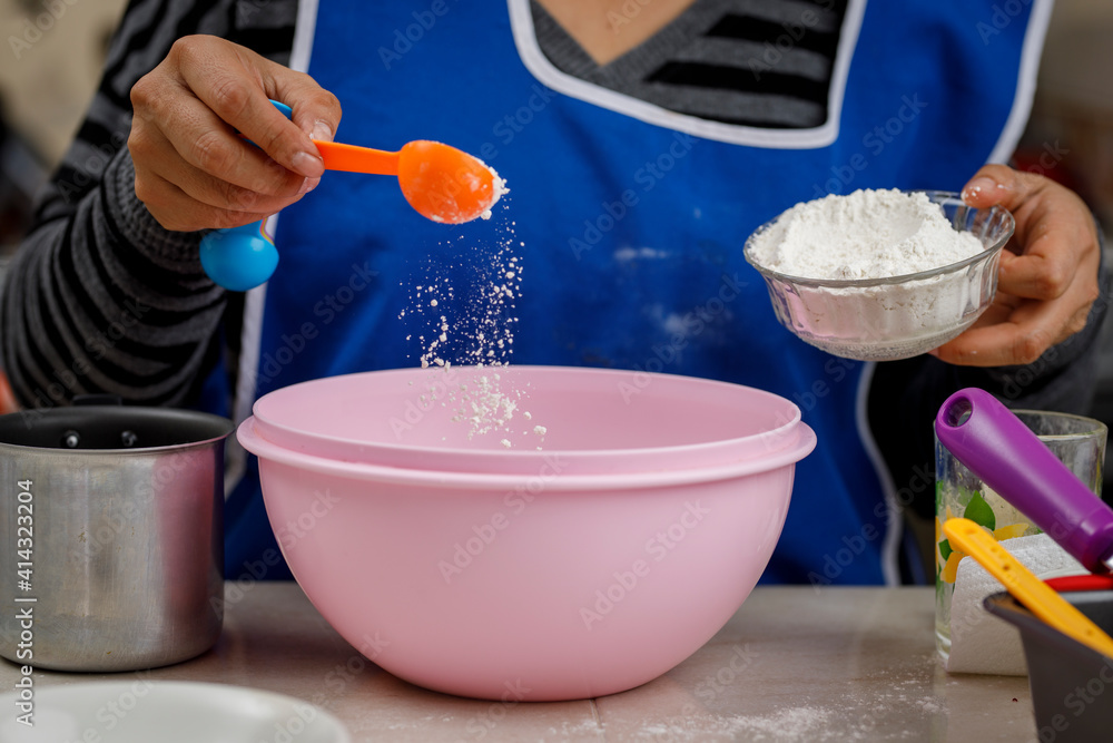 Agregando harina con una cuchara medidora a un recipiente, para ... Agregando harina con una cuchara medidora a un recipiente, para ...
