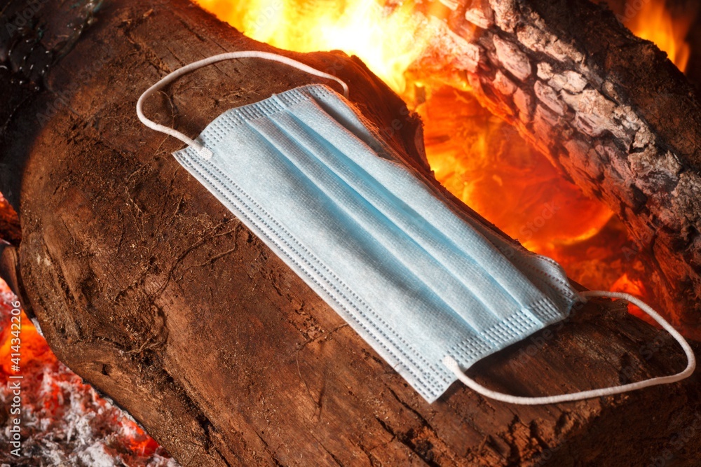 surgical mask burning on top of a log with fire, concept of ending ...
