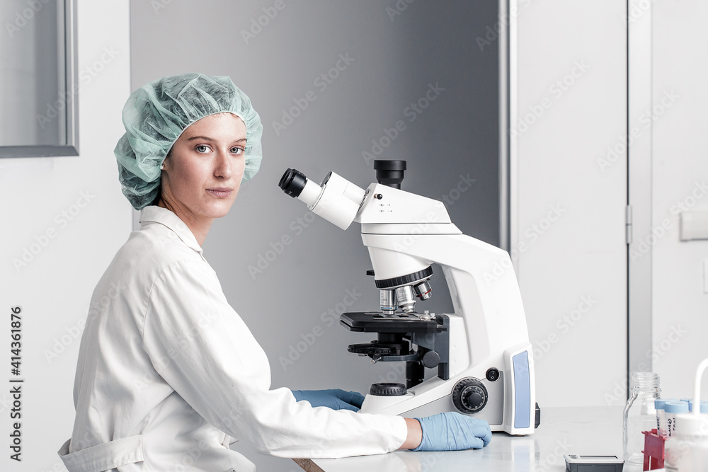 Softly tinted posed portrait of a female scientist under a microscope ...