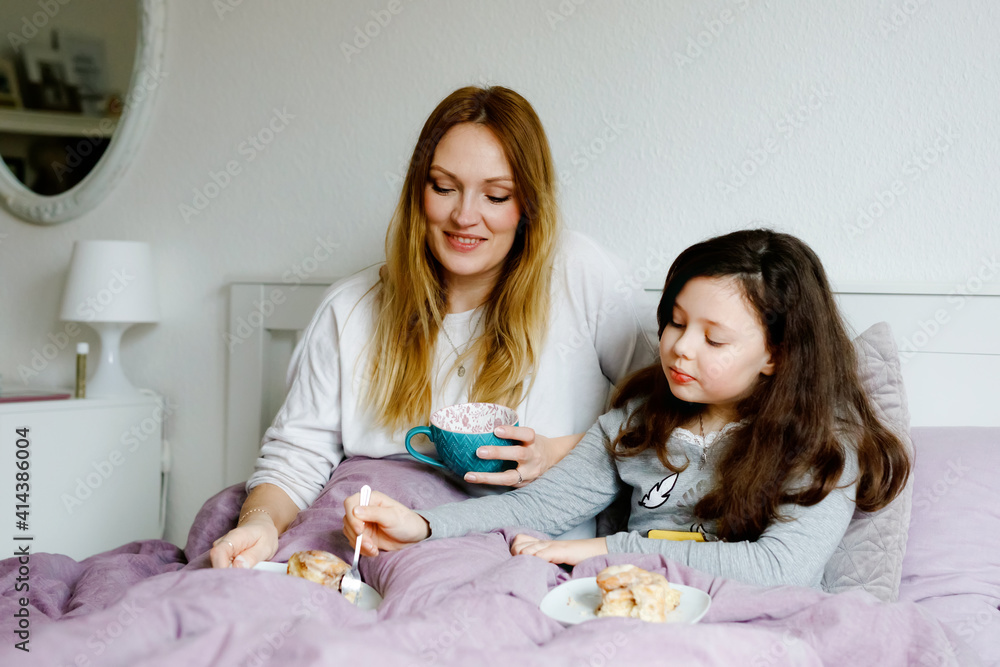 Lovely young mother and cute school kid girl cuddling together in bed ...