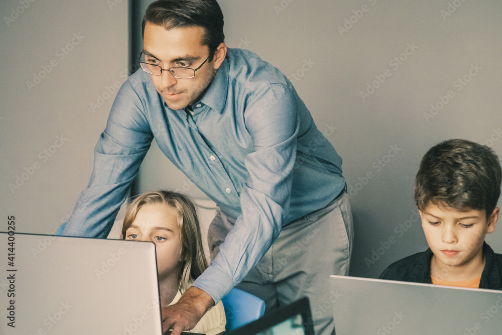 Focused teacher helping girl with task and typing on keyboard. Little ...