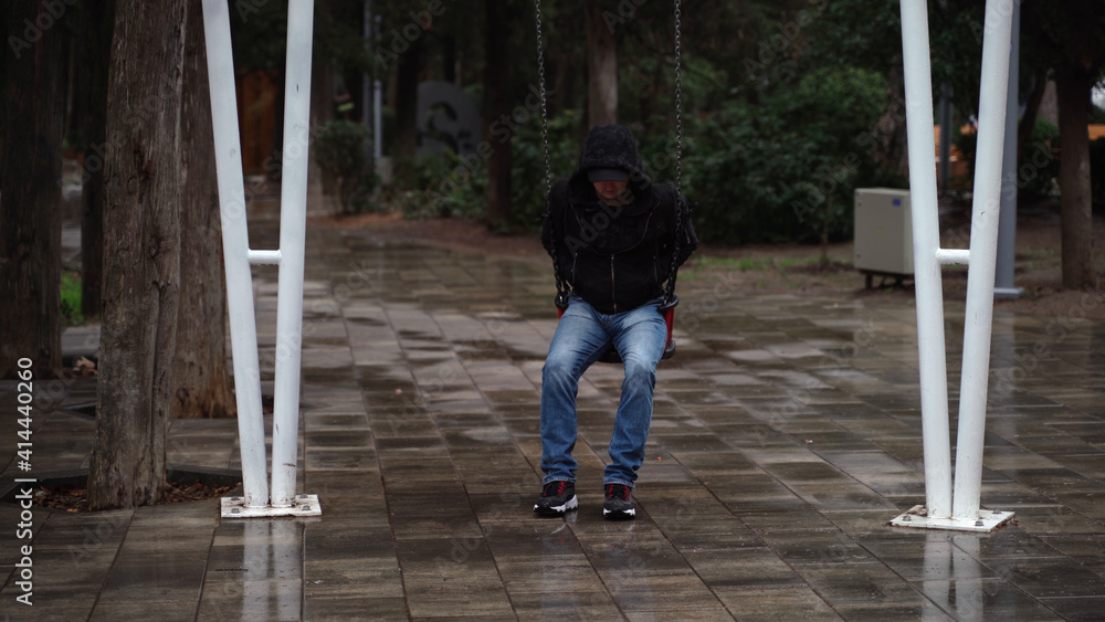 Lonely man in the park swinging on a swing. A sad man in depression is ...