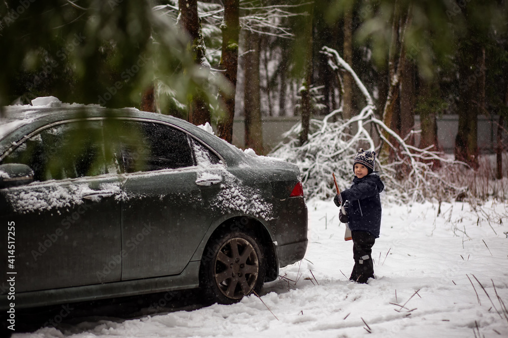 cute little boy helping to brush snow from a car on winter snowy day in ...
