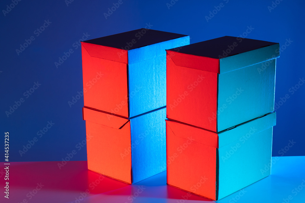 Large cardboard boxes in neon light. Four geared boxes on table ...