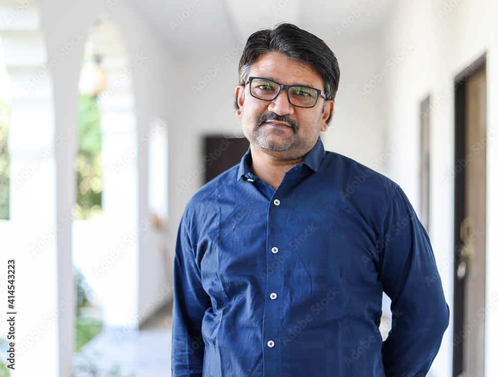 Portrait of a middle-aged Indian male with eyeglasses wearing a blue ...