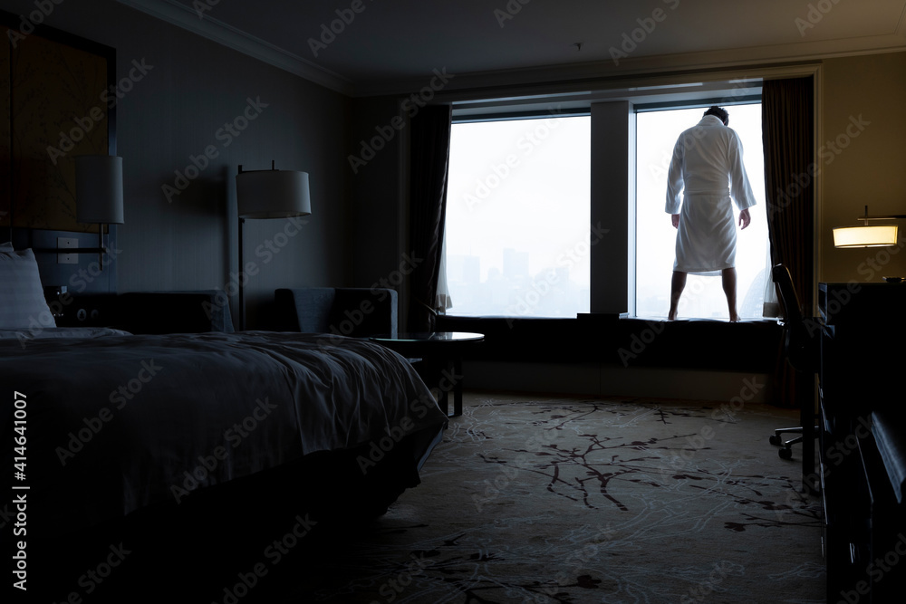 Unhappy man standing in window of hotel room, looking down to street ...