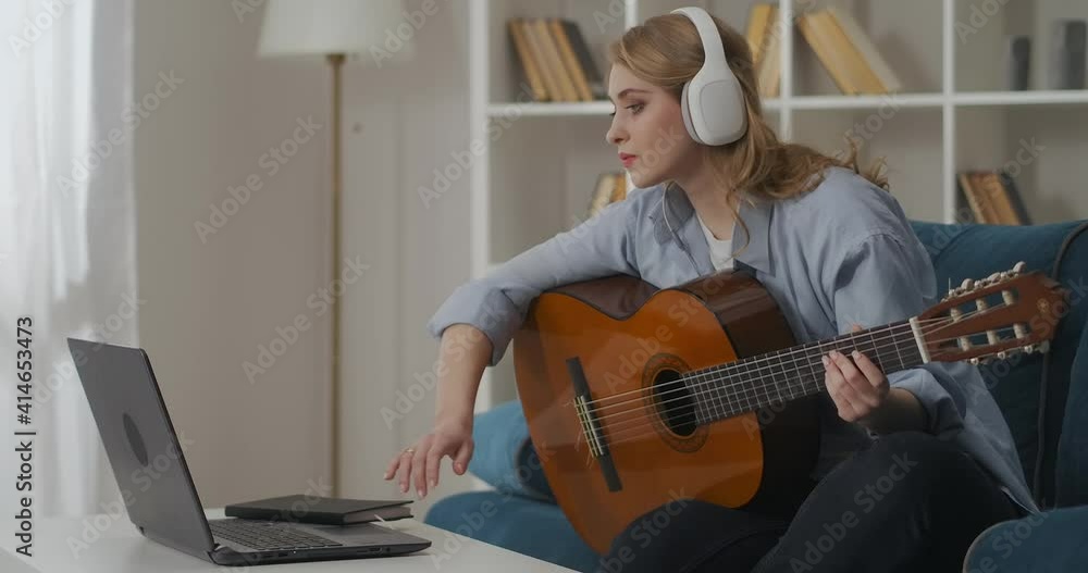female musician is playing guitar at home, listening to music by ...