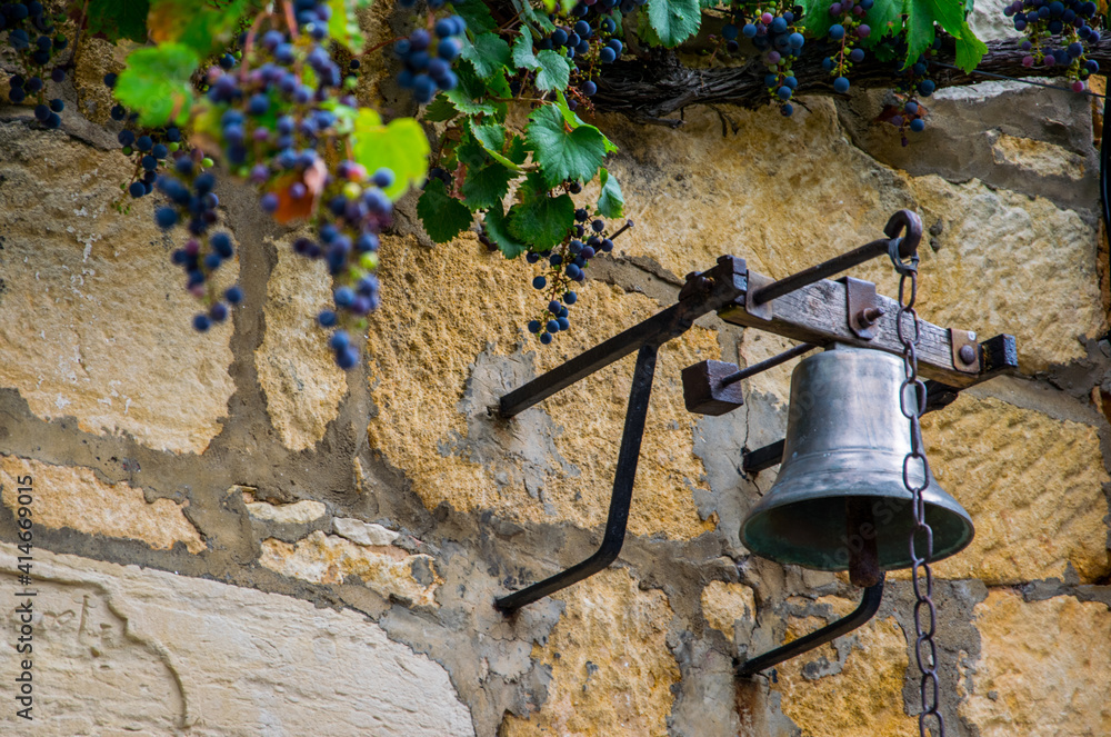 Campana y parra con uvas en una casa de piedra de una aldea histórica ...