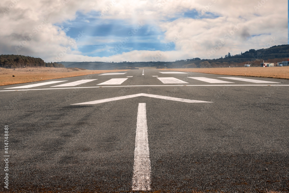 White arrow on a small asphalt air plane runway. Cloudy sky with small ...