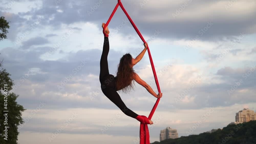 Female acrobat showing her flexibility and splits with red aerial silk ...