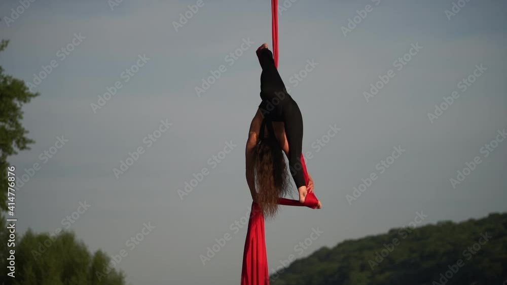 Female acrobat showing her flexibility and splits with red aerial silk ...
