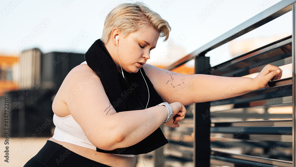 Side view of young plus-size woman looking at a smartwatch. Sweated and ...