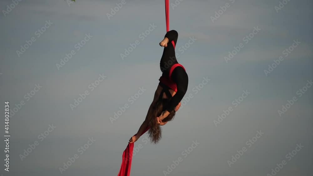 Female acrobat showing her flexibility and splits with red aerial silk ...