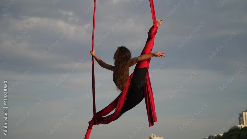 Female acrobat showing her flexibility and splits with red aerial silk ...