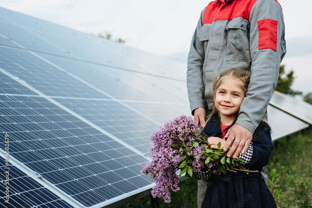 The child hugs the dad the electrician, on a background of solar panels ...