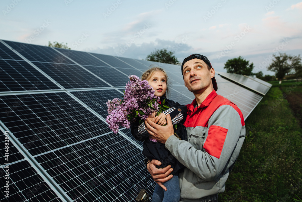 The child hugs the dad the electrician, on a background of solar panels ...